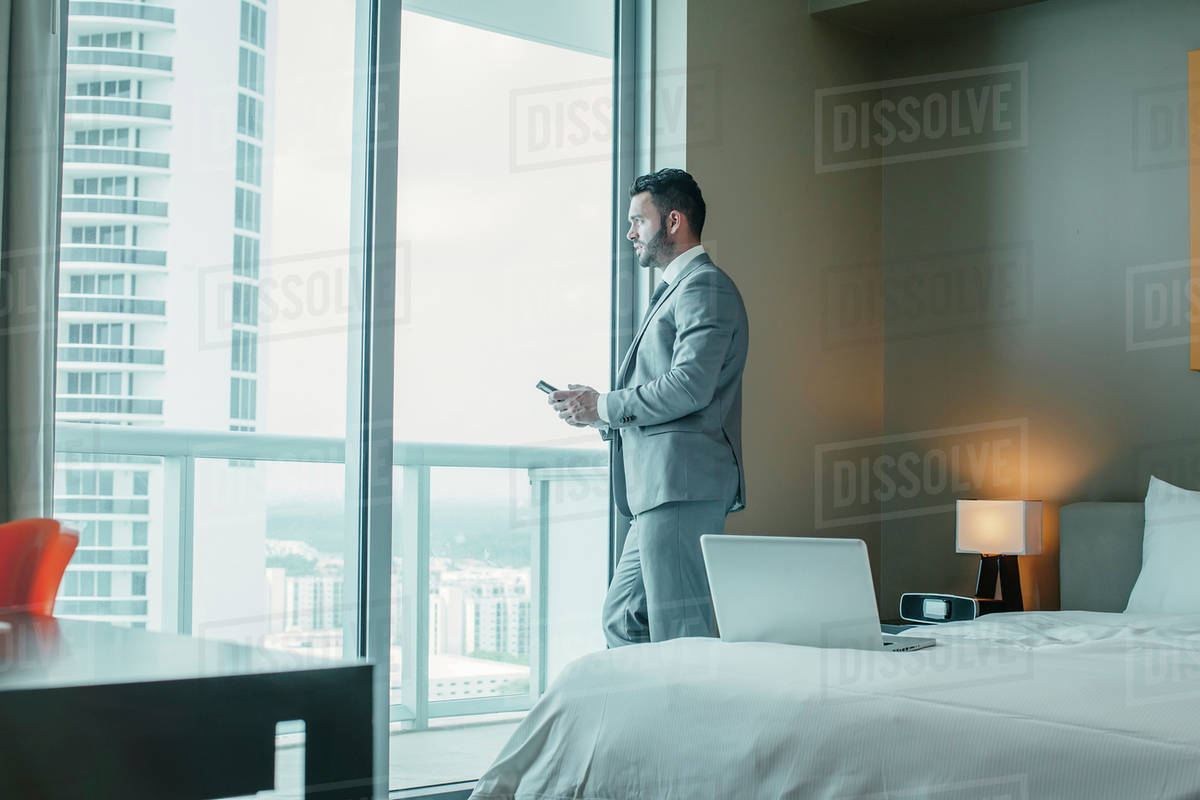 Businessman using cell phone at hotel window - Stock Photo - Dissolve