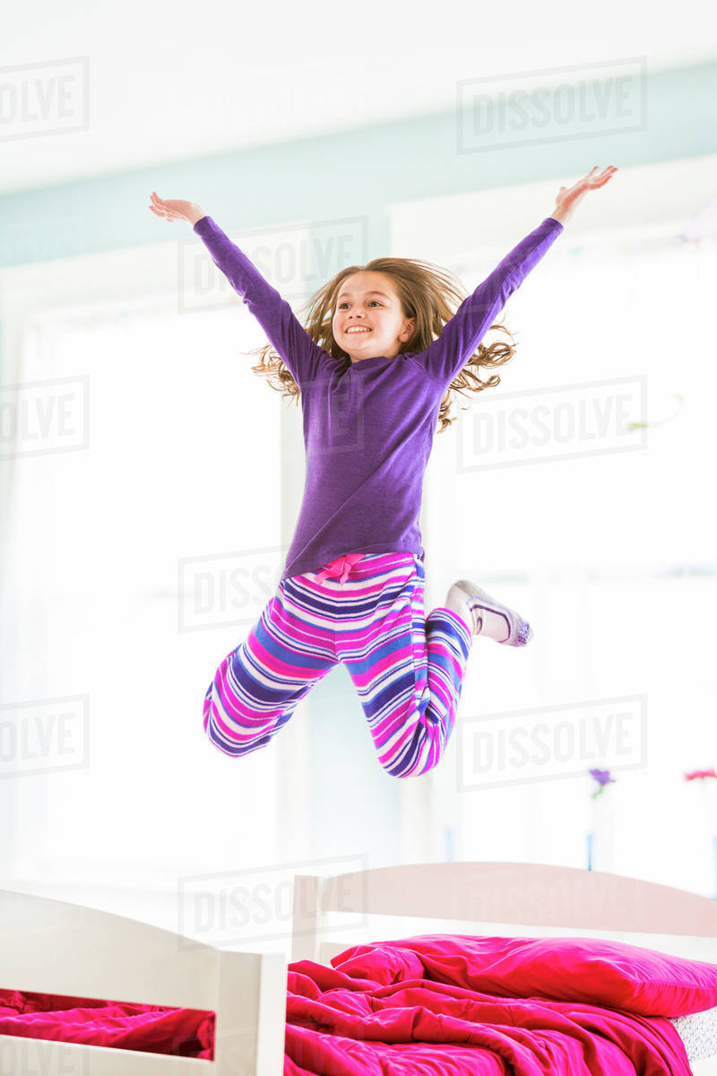 Caucasian girl jumping on bed - Royalty-free Stock Photo | Dissolve