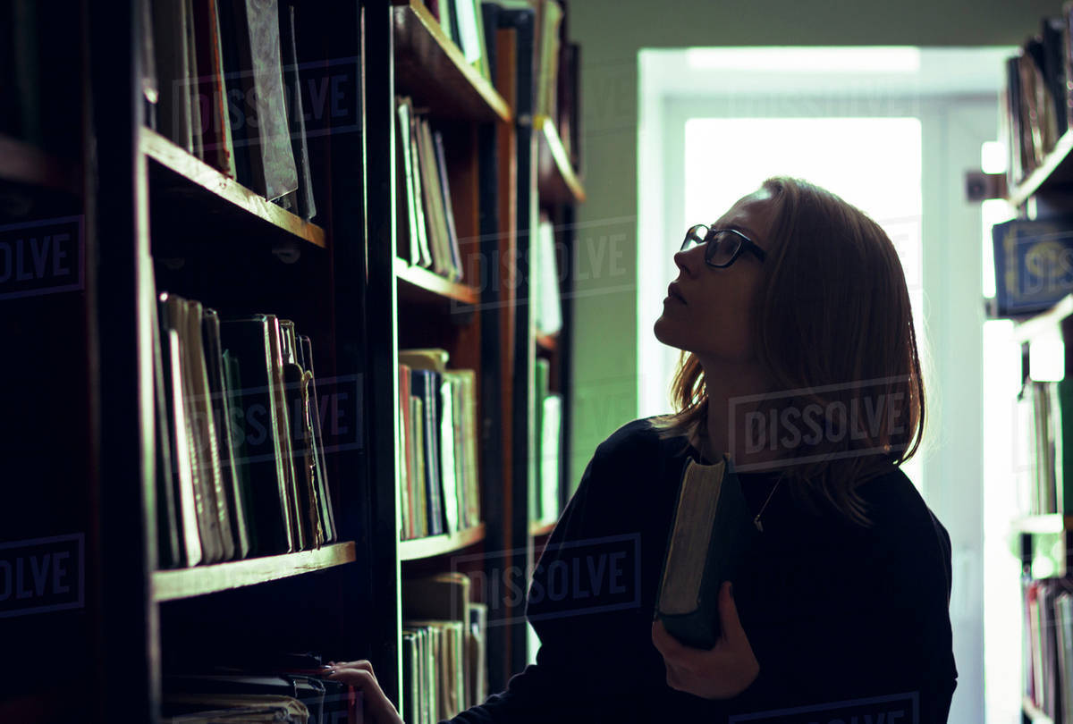 Caucasian woman searching for book in library - Royalty-free Stock ...