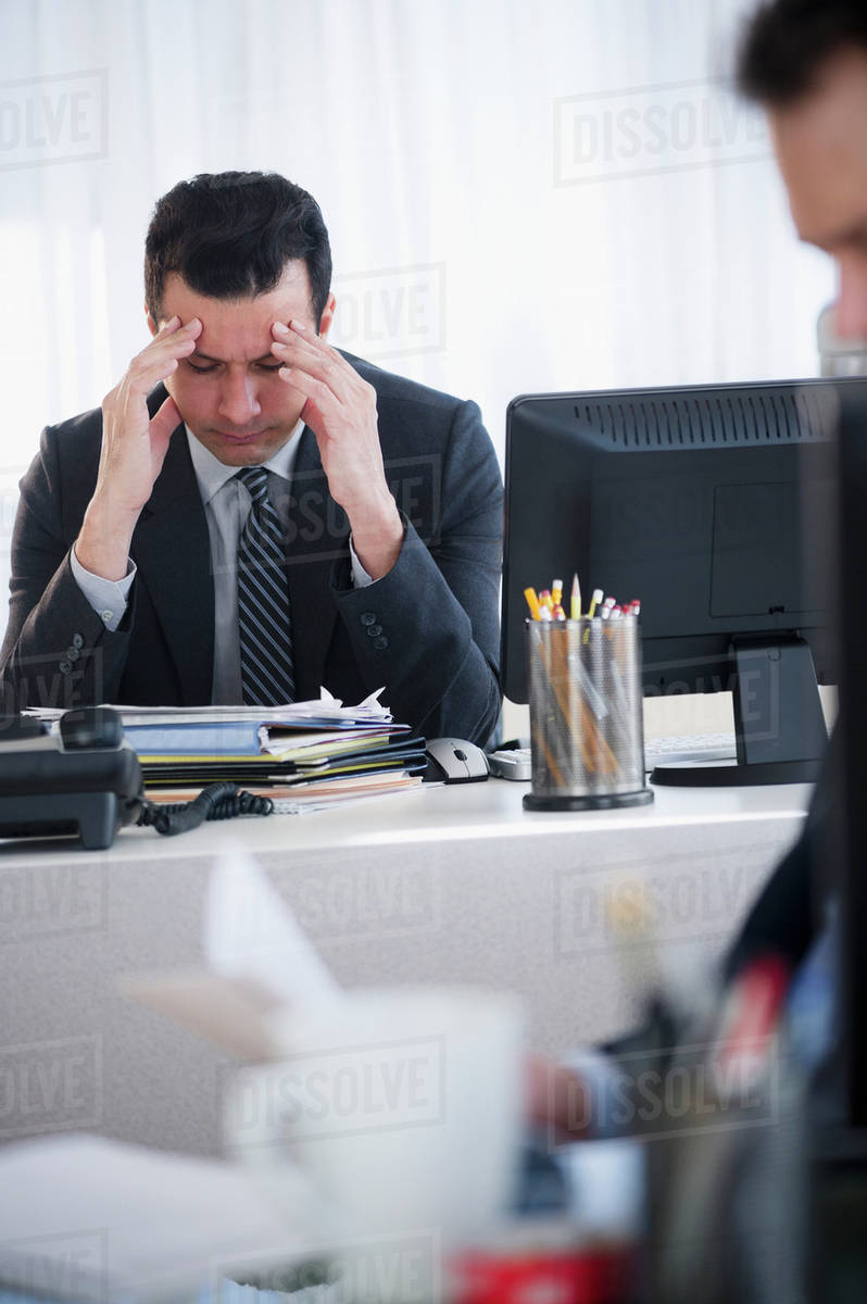 Mixed race businessman rubbing head at desk - Royalty-free Stock Photo ...
