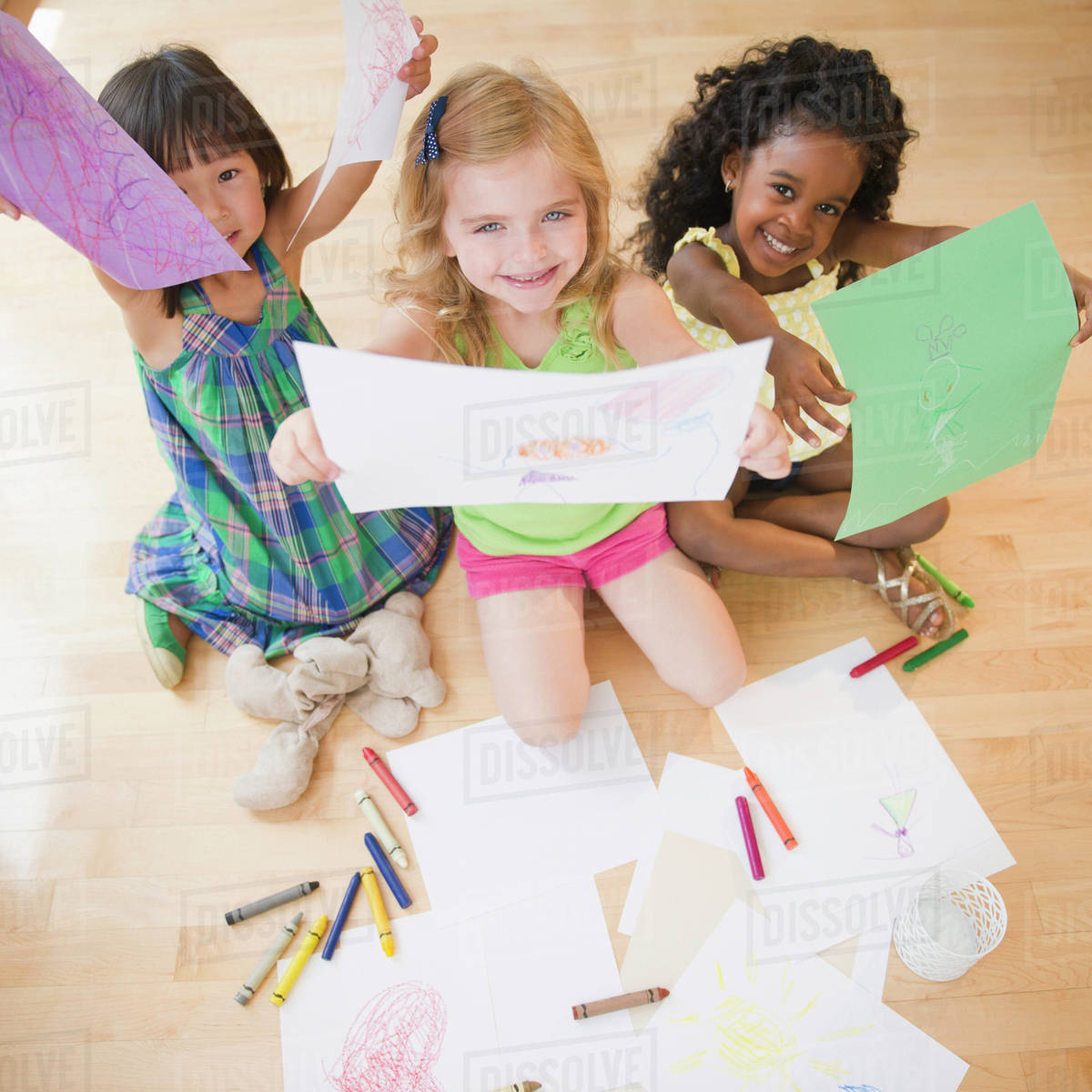 Children sitting on floor holding up drawings - Stock Photo - Dissolve