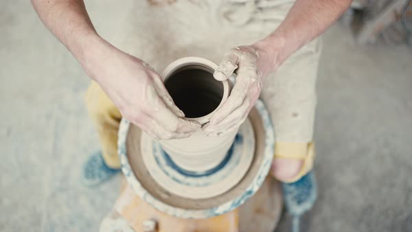 Top view of potter smoothing out and forming ceramic vase on pottery ...
