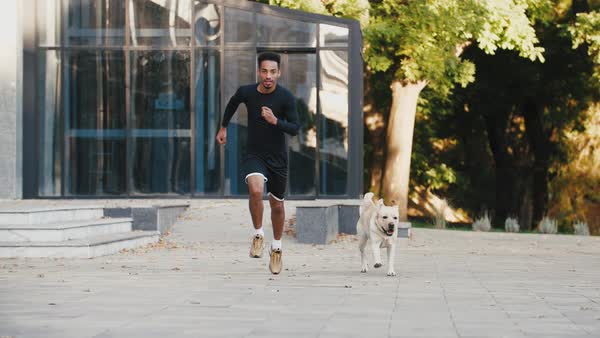 Young black man running with his white labrador dog through the city ...