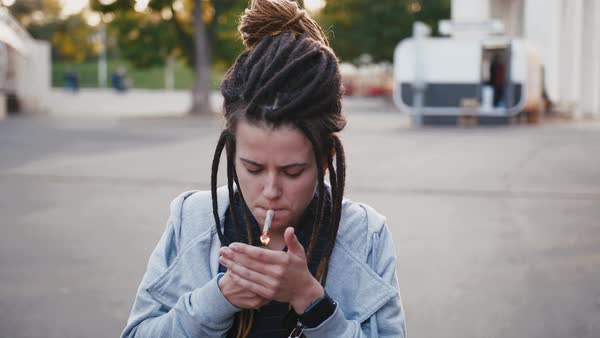 Young woman with dreadlocks smoking marijuana joint in park - 4K ...