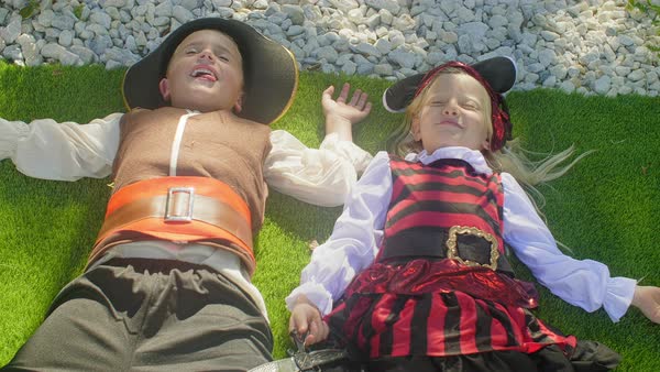 Two children in pirate costumes falling back onto ground playing dead ...