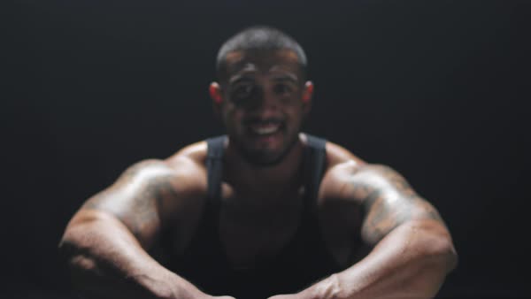 Zooming shot of a muscular man sitting down smiling at the camera on a ...