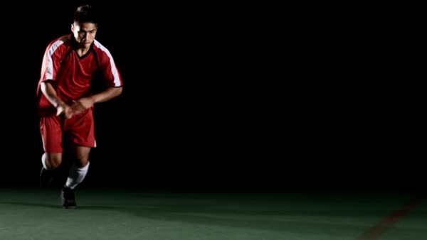 Wide shot of a soccer player approaching the ball and kicking it with ...