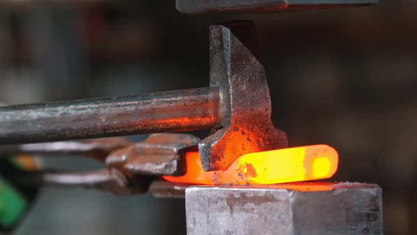 Blacksmith cutting the piece of incandescent metal with an axe and ...