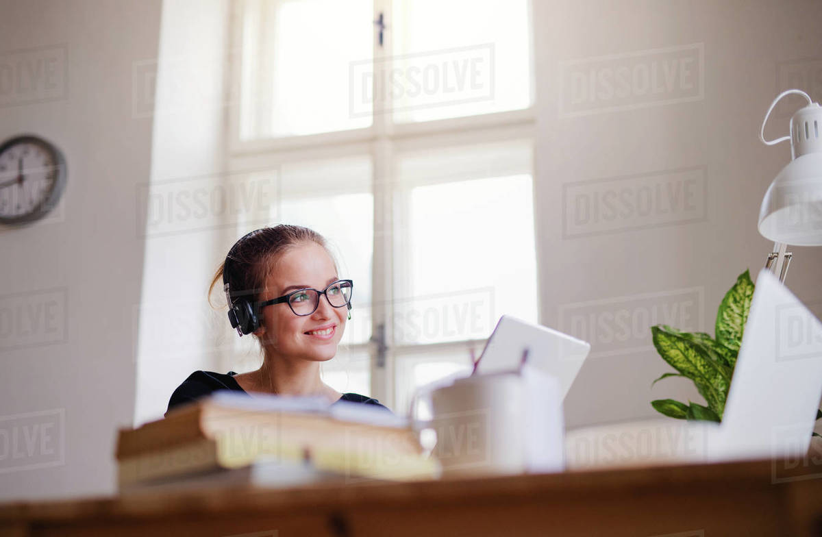 A young happy college female student sitting at the table at home ...