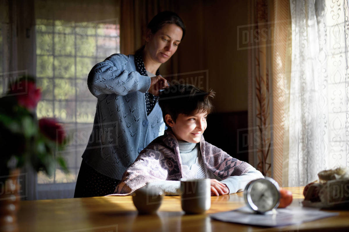Portrait of sad poor woman cutting daughter's hair indoors at home ...