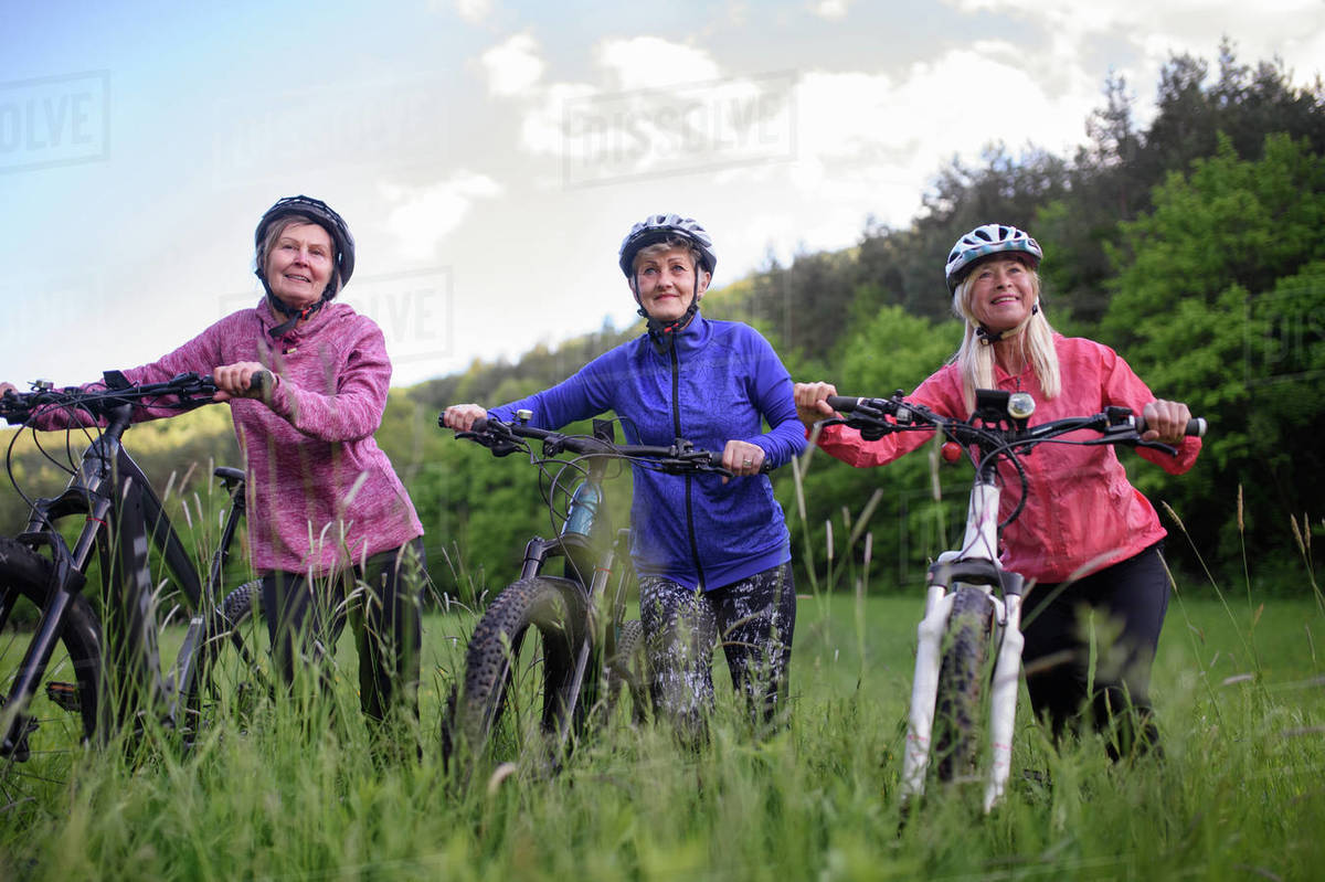 Happy active senior women friends cycling together outdoors in nature ...