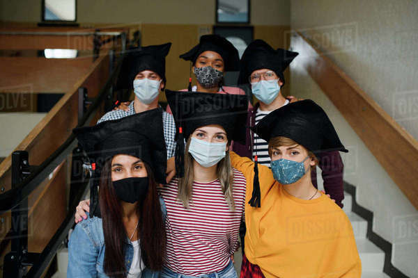 Front view of young students with face masks and graduation caps back ...