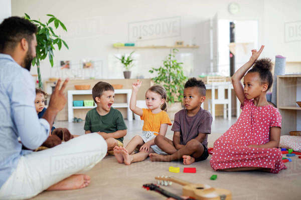 A group of small nursery school children sitting on floor indoors in ...