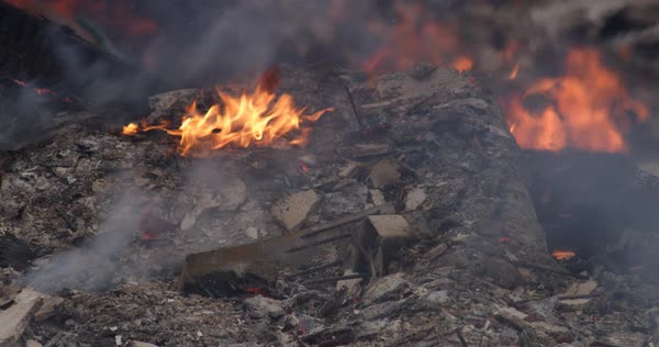 Close-up low flames burning in ash-covered rubble after a structure ...