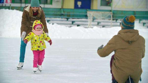 Happy family at the skating rink. Child learning to skate with their ...