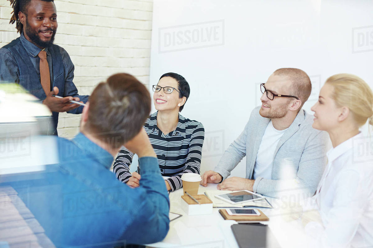 Group of executives at conference table in office listening intently to ...