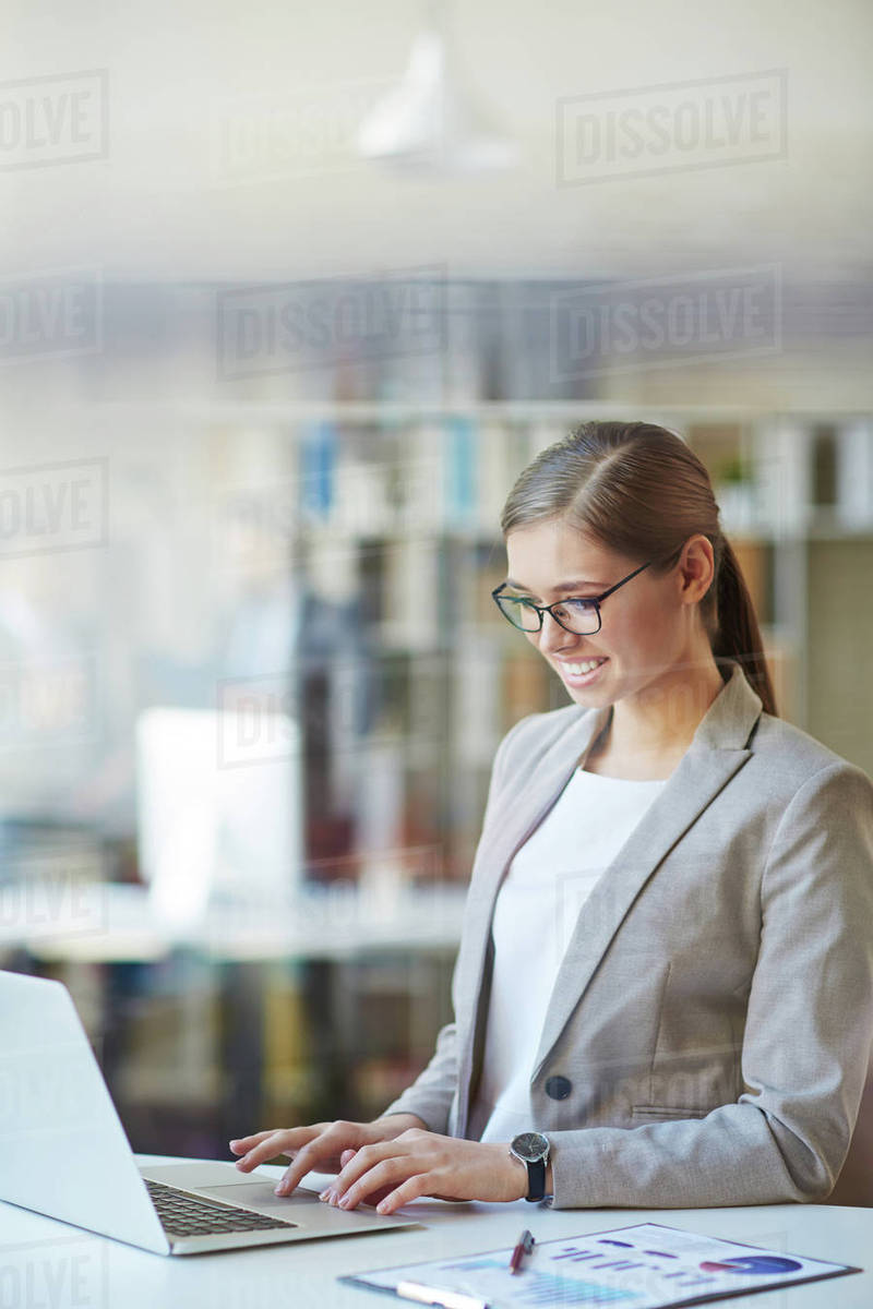 Smiling young office worker using laptop for work - Royalty-free Stock ...