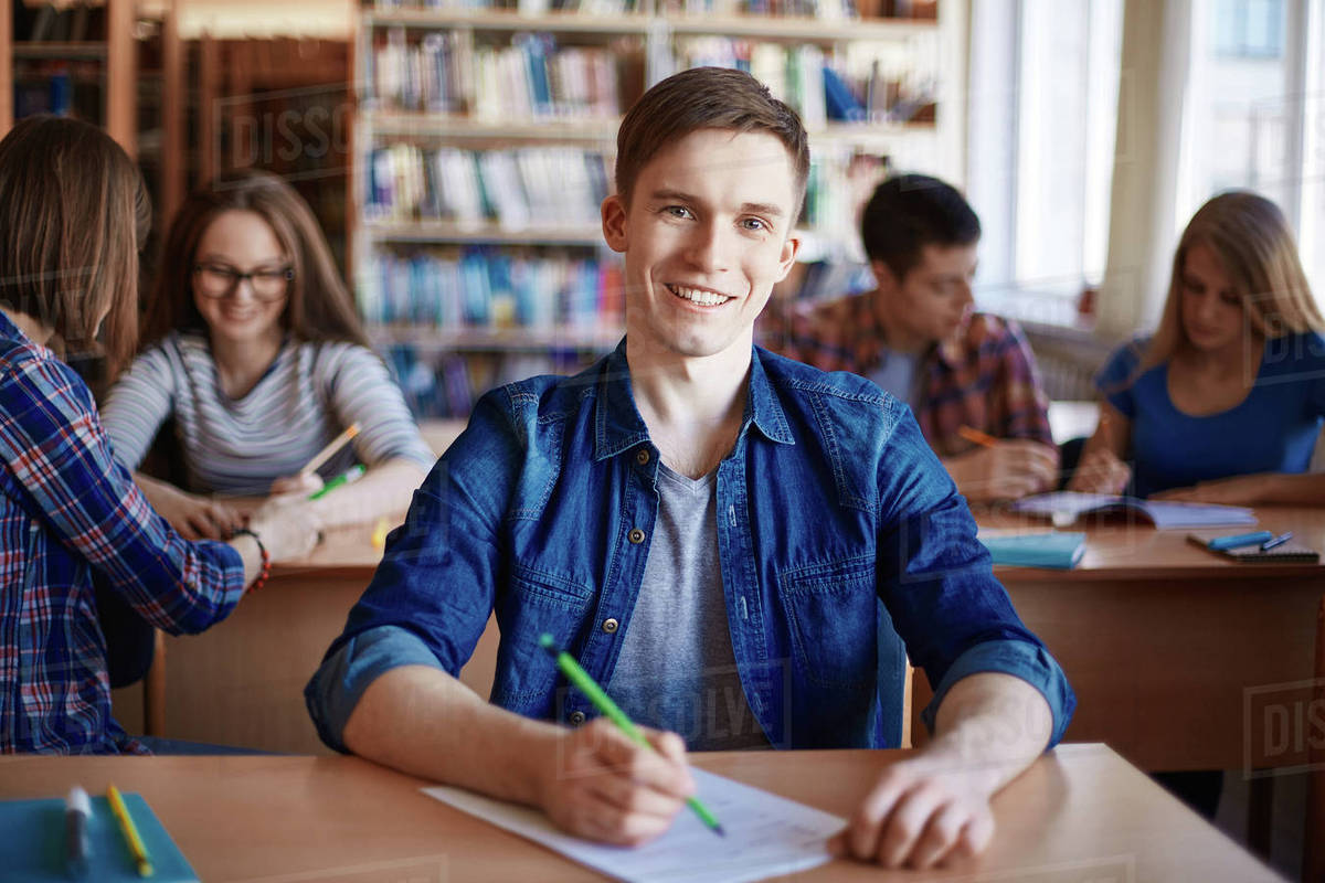 Happy student looking at camera by desk - Royalty-free Stock Photo ...