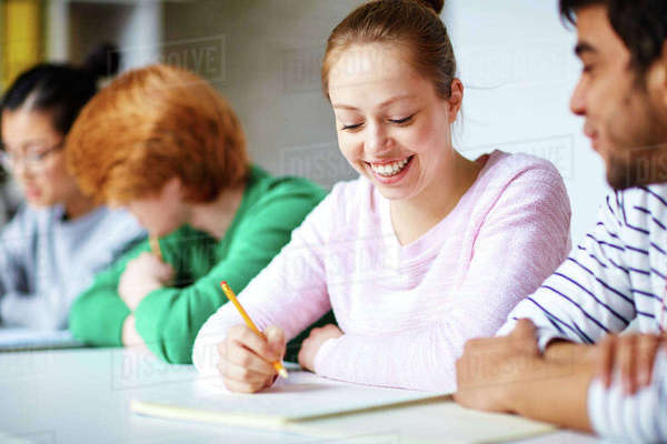 Smiling female student sitting at the table and making notes in her ...