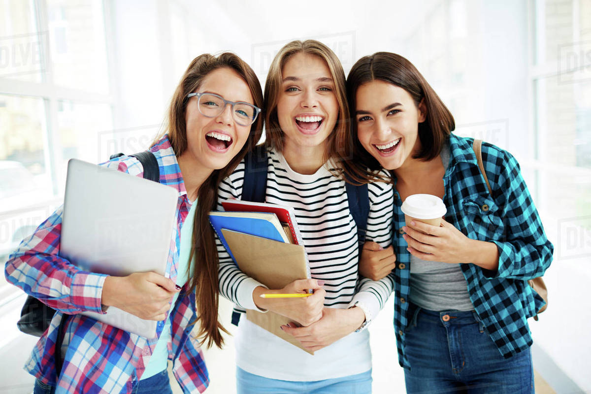 Portrait of happy students standing together with laptop and notebooks ...