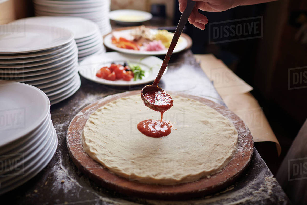 Chef pouring tomato sauce on flat-bread for pizza - Stock Photo - Dissolve