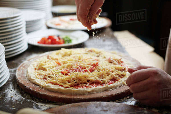 Chef sprinkling grated cheese on pizza top - Stock Photo - Dissolve