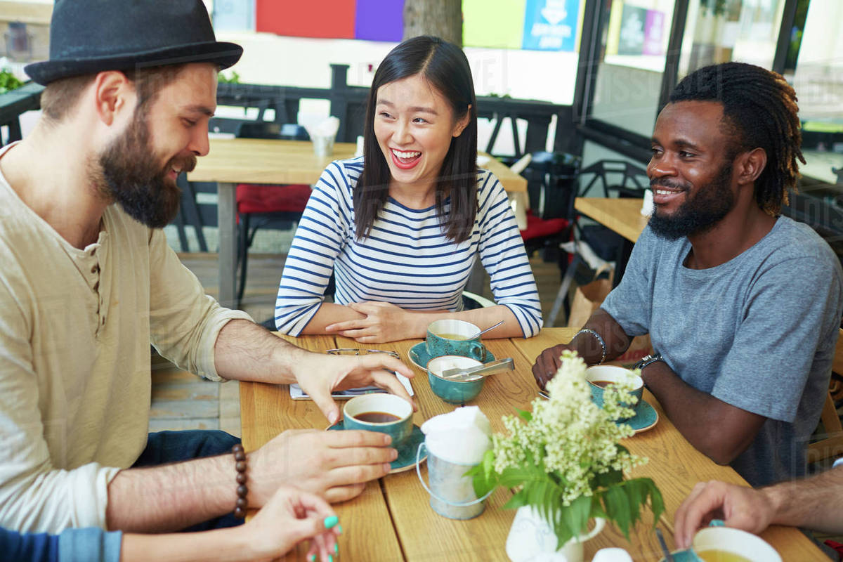 Three friends laughing during conversation in cafe - Stock Photo - Dissolve