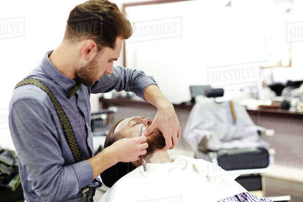 Barber shaving beard of client with blade - Stock Photo - Dissolve