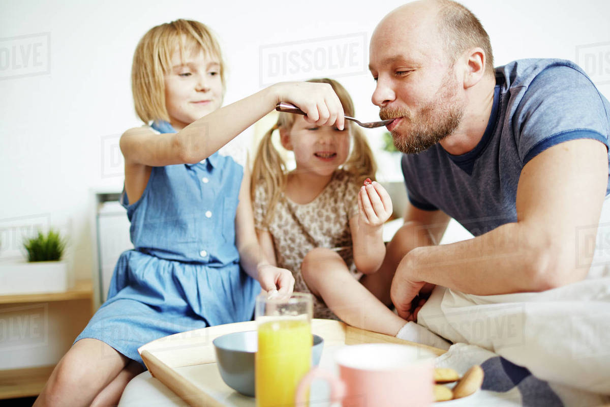 Little girl feeding her dad from spoon in the morning of father day ...