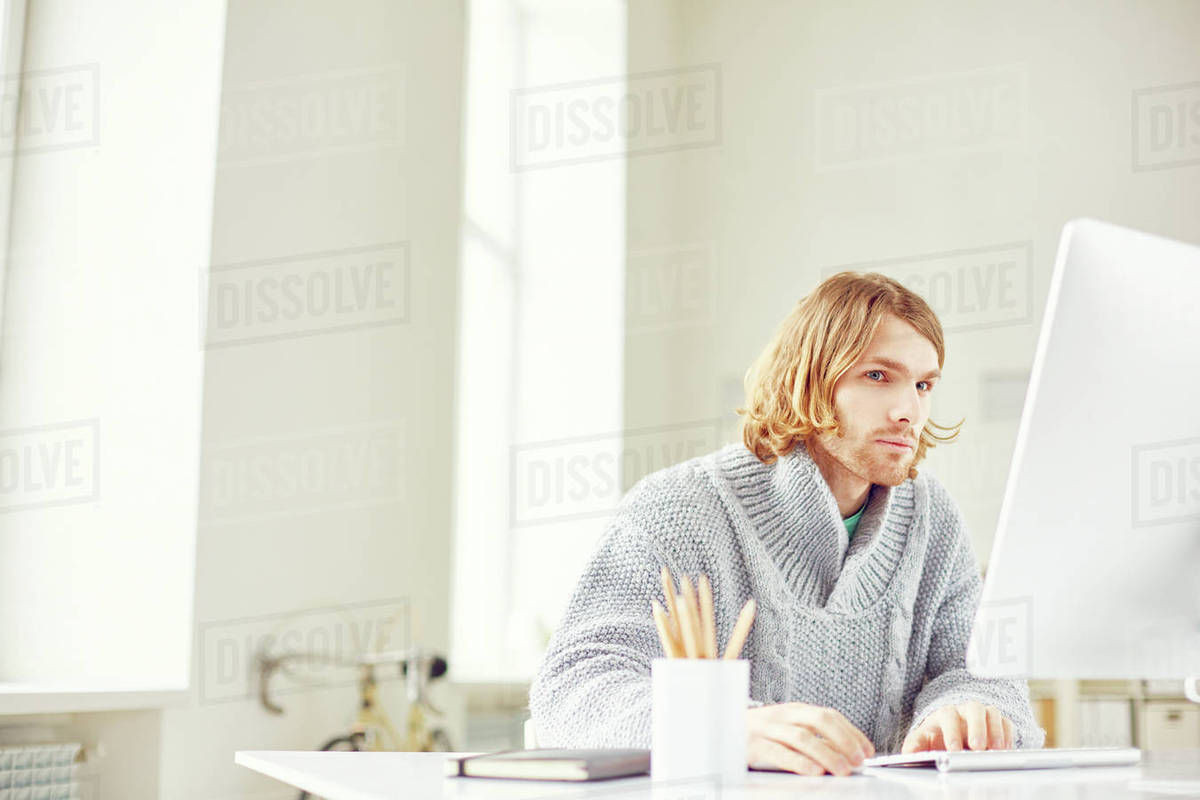 Man in sweater sitting at computer - Stock Photo - Dissolve