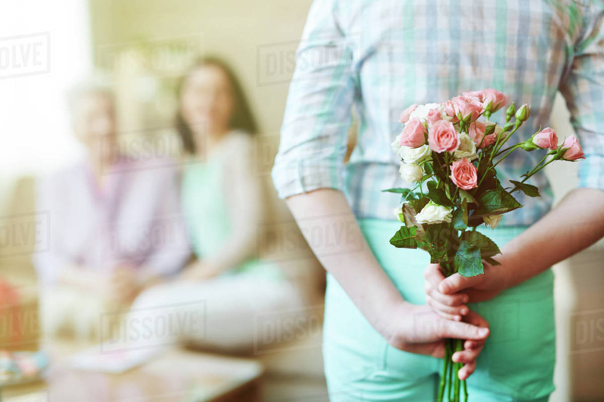 Rear view of young girl holding bunch of roses for her mother in the ...