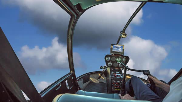 Helicopter cockpit flying in a blue cloudy sky, with pilot arm in ...