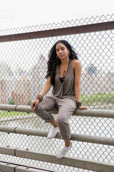Young woman sitting on a railing on a bridge - Stock Photo - Dissolve