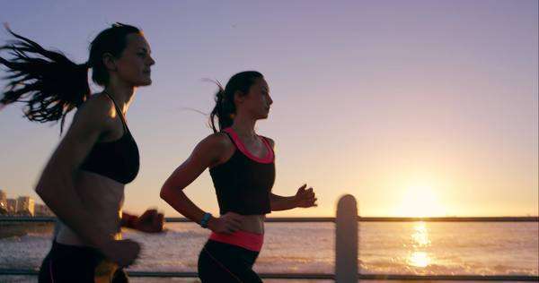 Two athletic woman running outdoors in slow motion on promenade at ...
