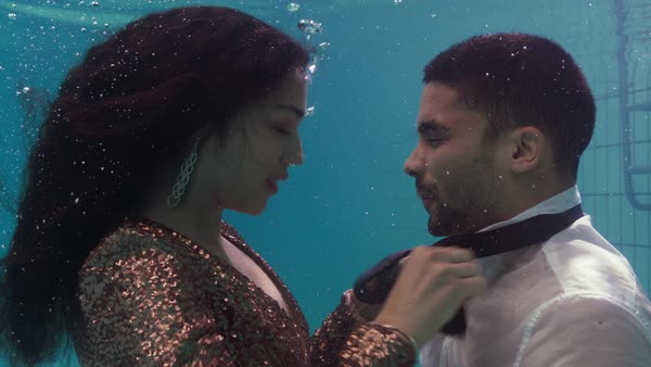 Romantic couple kissing underwater in swimming pool wearing clothes ...