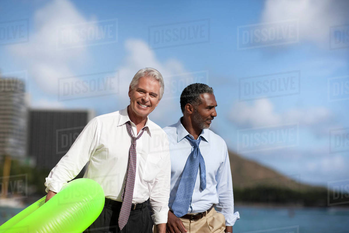 Portrait of a smiling businessman relaxing on a beach with a colleague ...