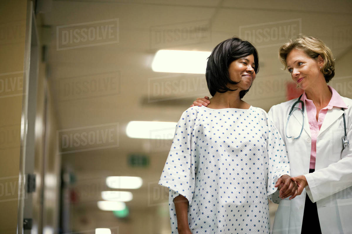 Doctor helping her patient to walk down the corridor for the first time ...