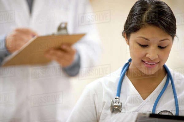 Portrait of young female nurse writing on a clipboard, with a male ...