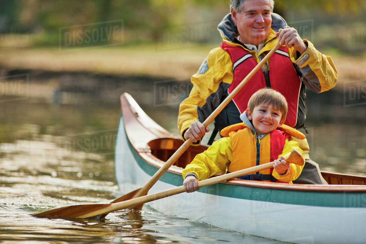 Happy grandfather and young grandson canoeing together on a lake ...