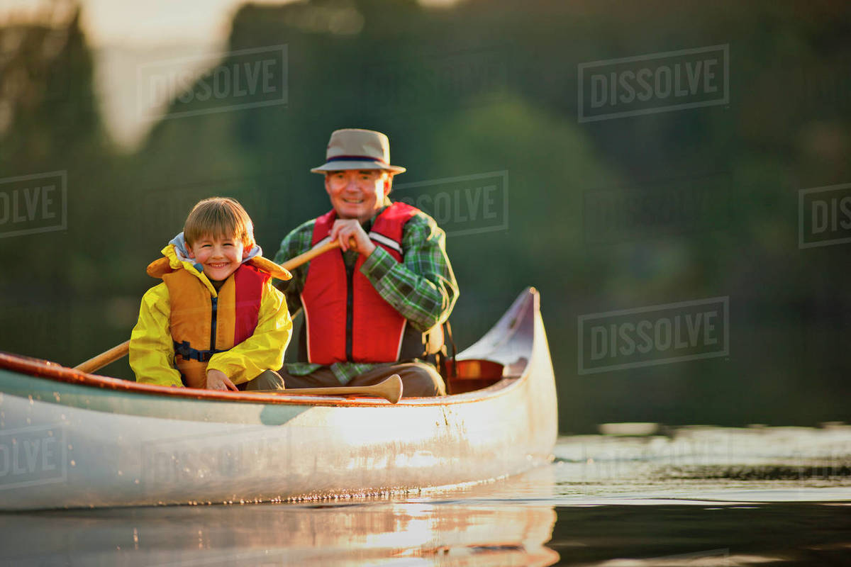 Happy grandfather and young grandson canoeing together on a lake ...