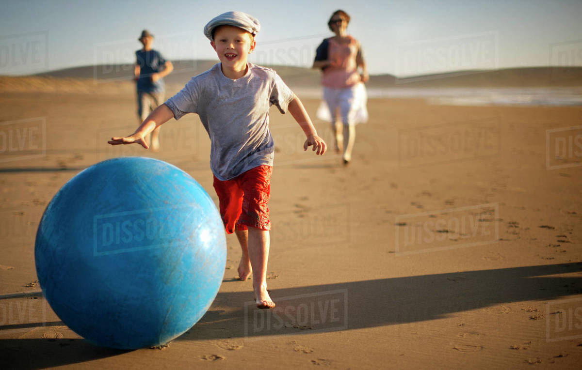 Portrait of a smiling young boy chasing a swiss ball along a sandy ...