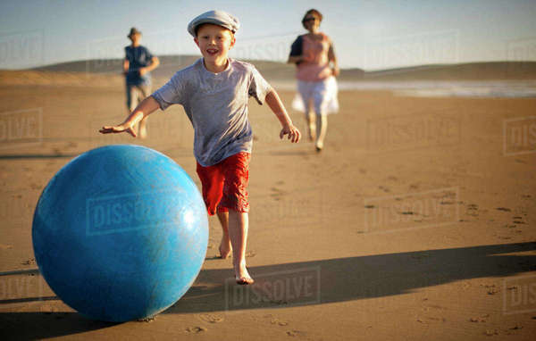 Portrait of a smiling young boy chasing a swiss ball along a sandy ...