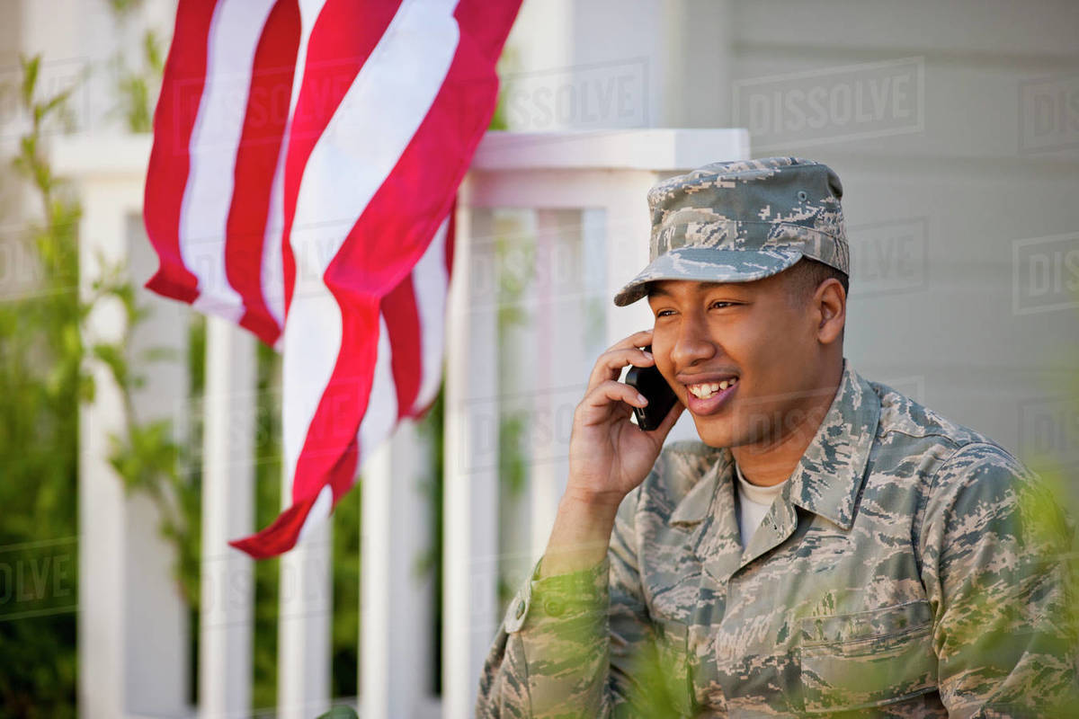 Smiling young army soldier talking on a cell phone outside his home ...