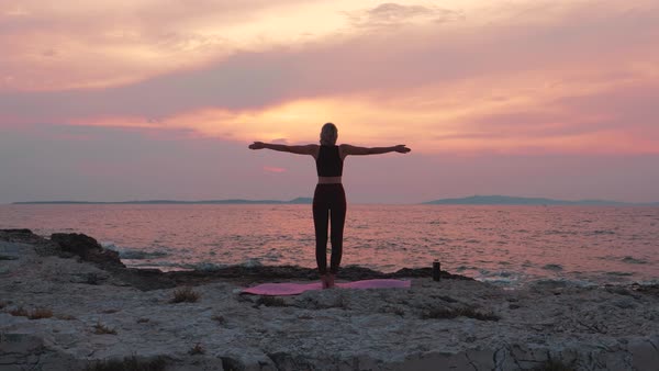 Wide shot of a young woman doing namaste pose before starting her yoga ...