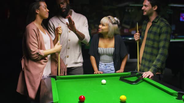 Diverse group of friends in a pool hall looking and smiling to camera ...