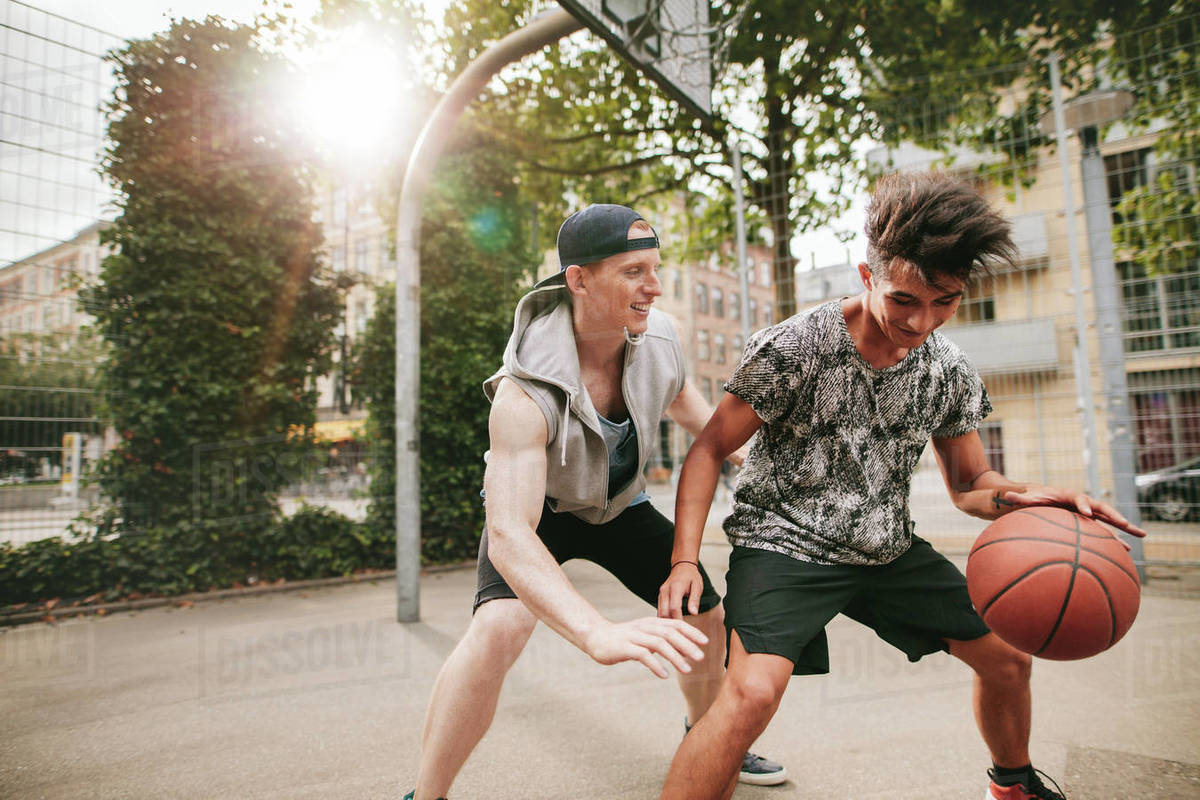 Two young friends playing basketball on court outdoors and having fun ...