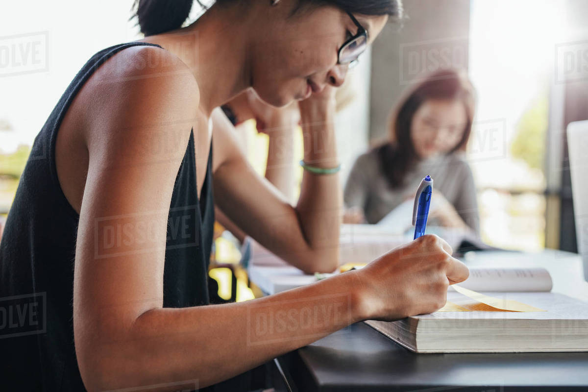 Close up shot of young female students writing notes with classmates ...