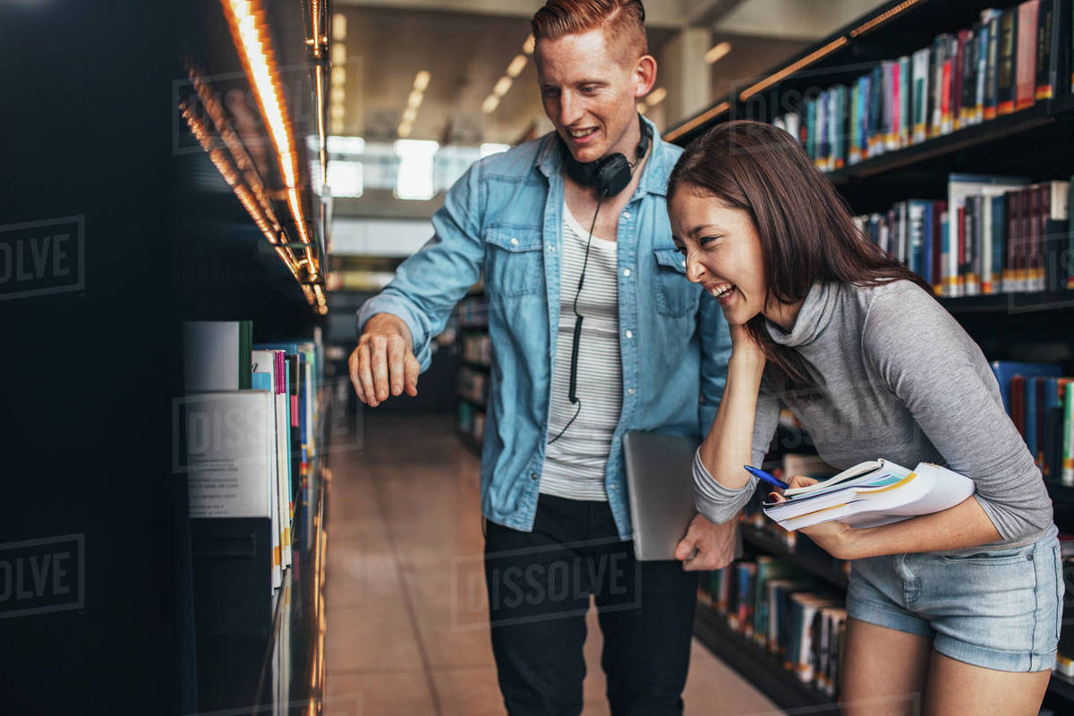 Image of happy young man and woman standing by book shelf in library ...