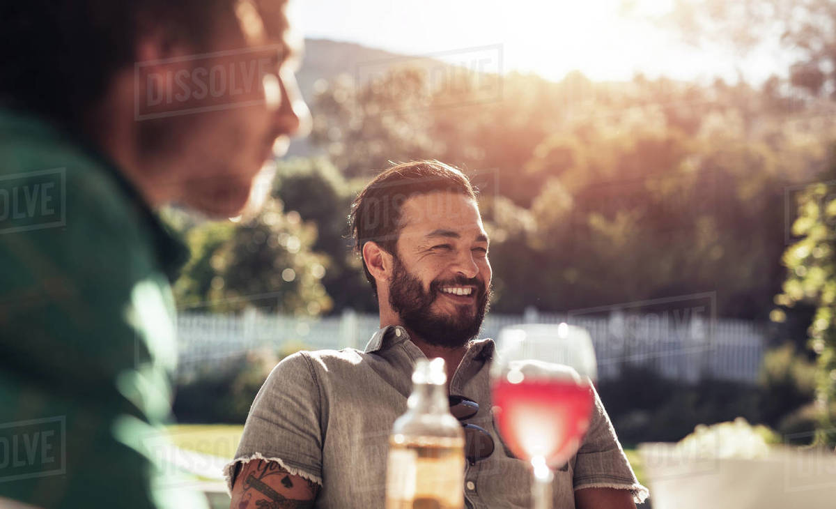 Shot of young man sitting outdoors with friends smiling. People ...