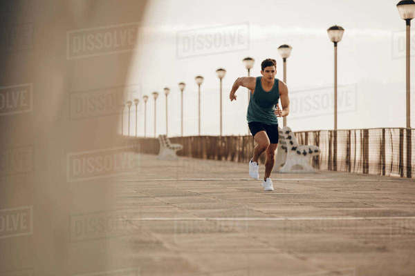 Full length shot of fit young man running fast on the promenade. Male ...